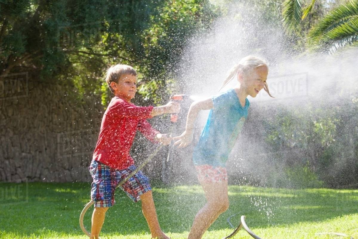 Boy splashing girl in garden with water sprinkler - Royalty-free Stock ...