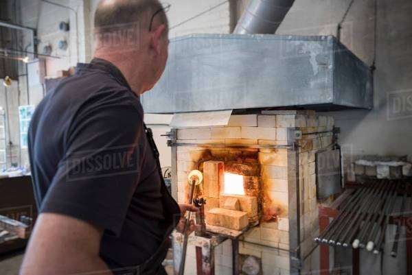 Glassblower drawing molten glass from furnace - Stock Photo - Dissolve