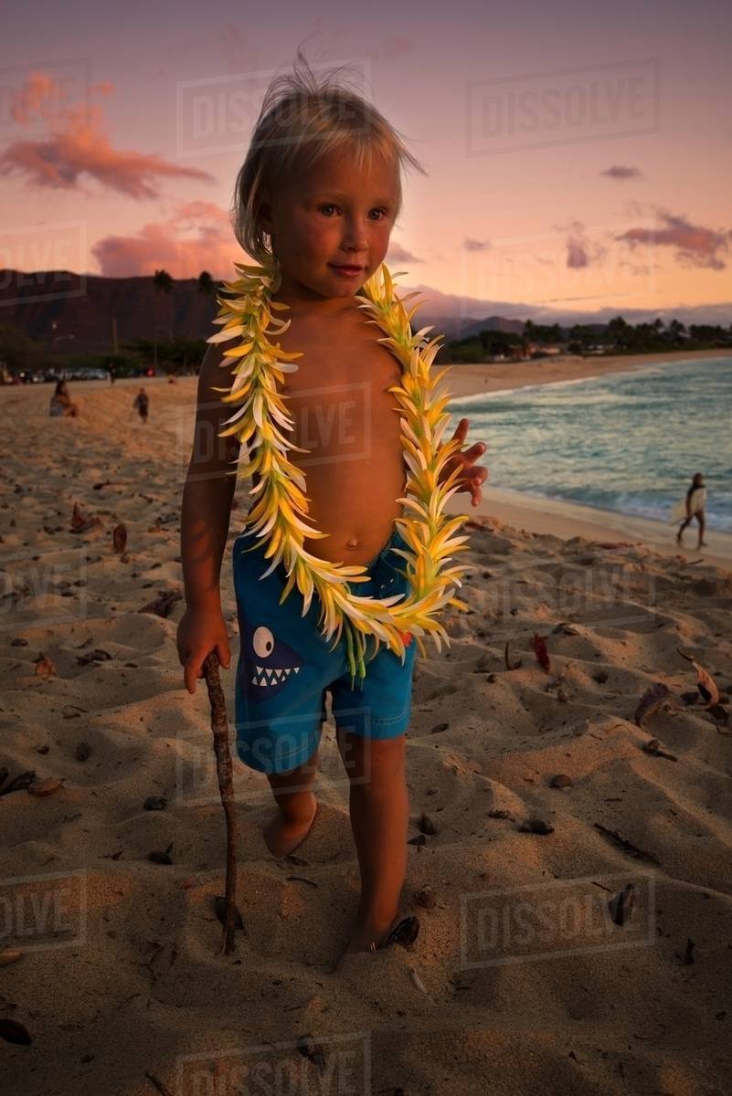 Young boy, wearing hawaiian garland, walking along beach, Makaha, Oahu ...
