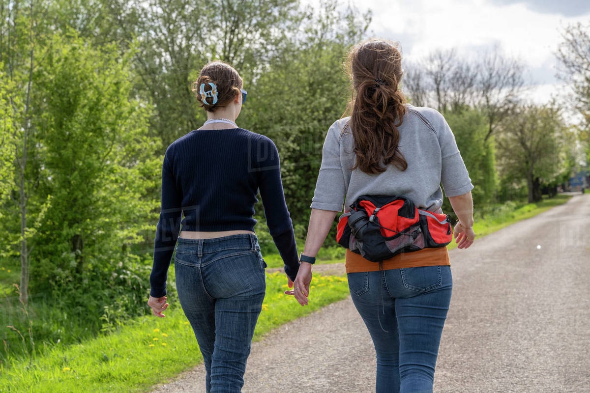 Two people walking side by side on a sunny pathway surrounded by green ...
