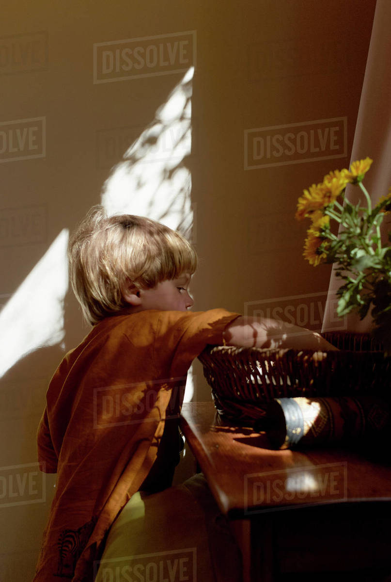 Young child reaching into a wicker basket near a vase of yellow flowers ...