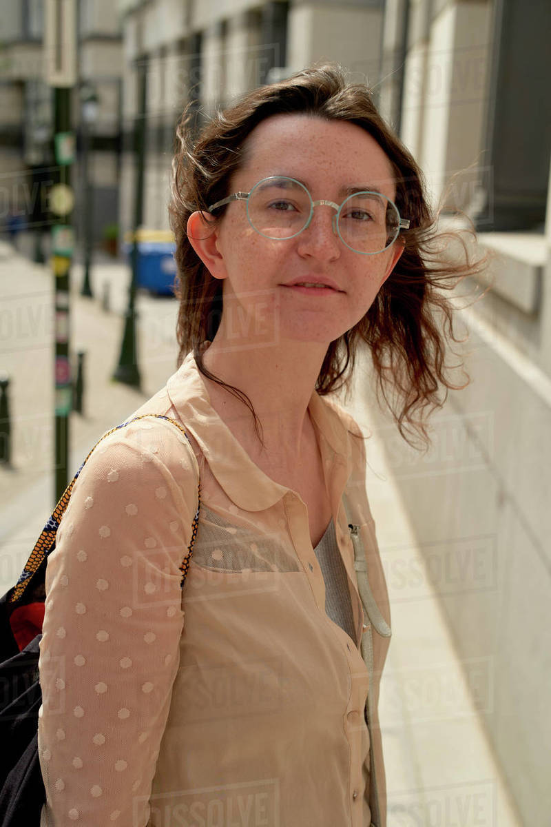A confident young woman with glasses and wind-swept hair smiles while ...