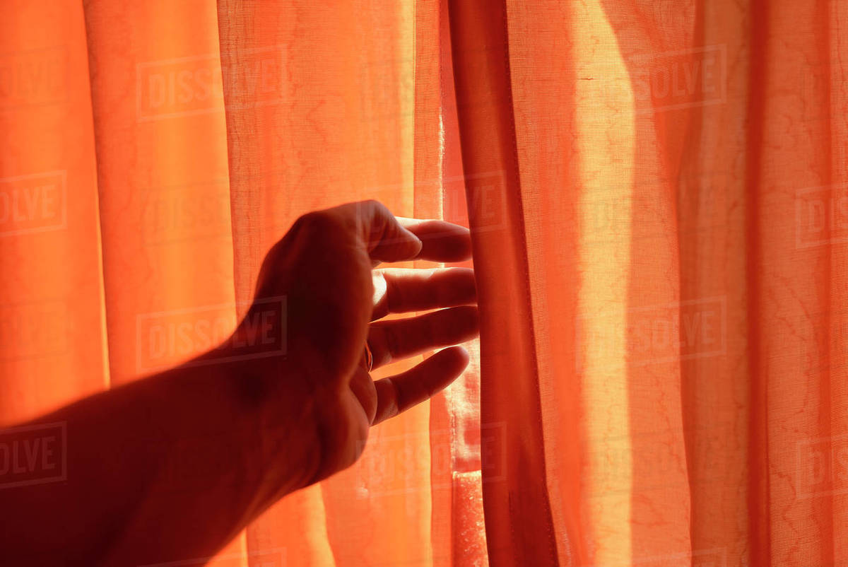 A hand is parting an orange curtain in a cargo ship cabin to let in ...
