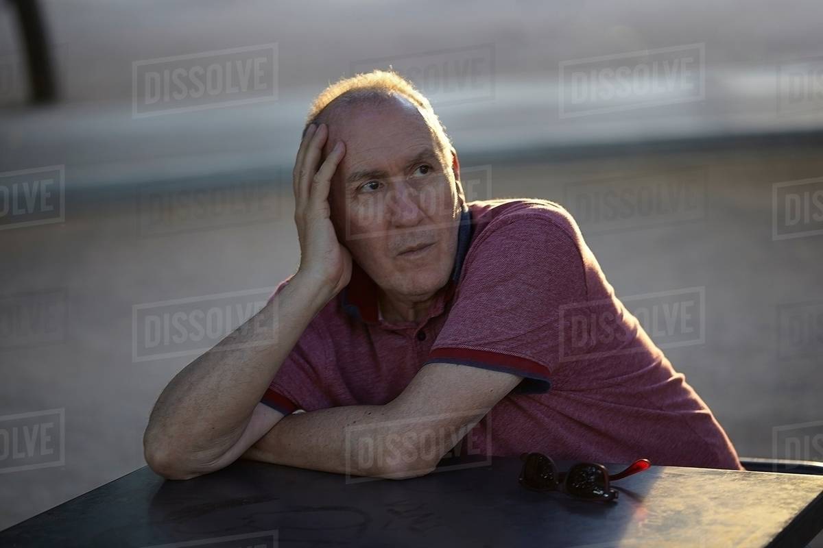 Senior man sitting at table, resting on elbow - Stock Photo - Dissolve
