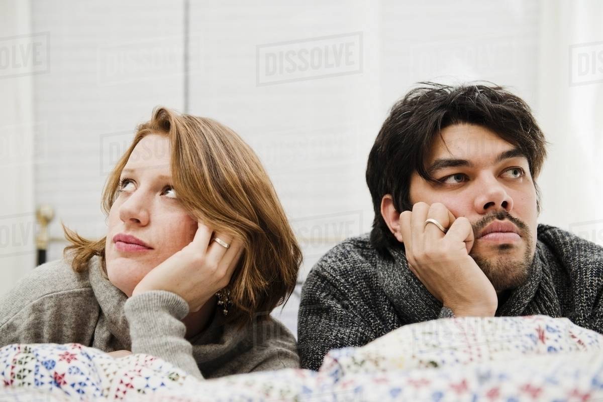 Couple resting chins in hands on bed - Royalty-free Stock Photo | Dissolve