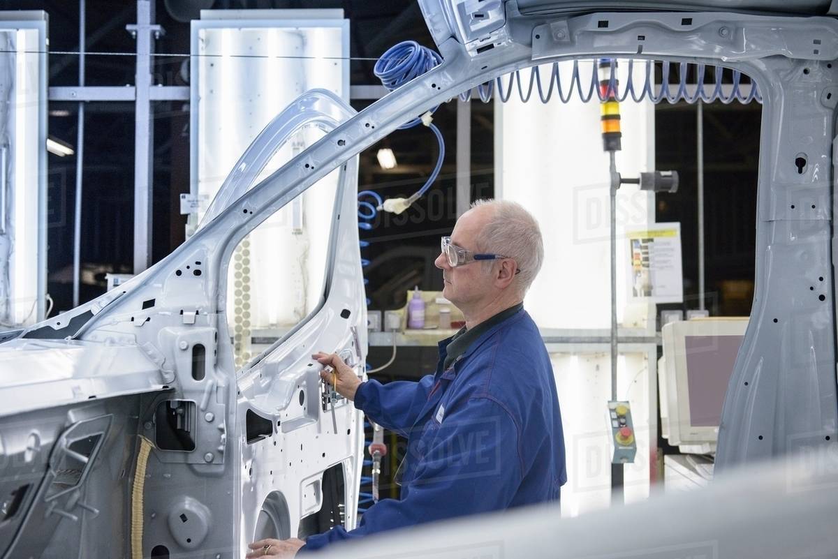 Worker inspecting paint finish of vehicle in inspection station in car ...