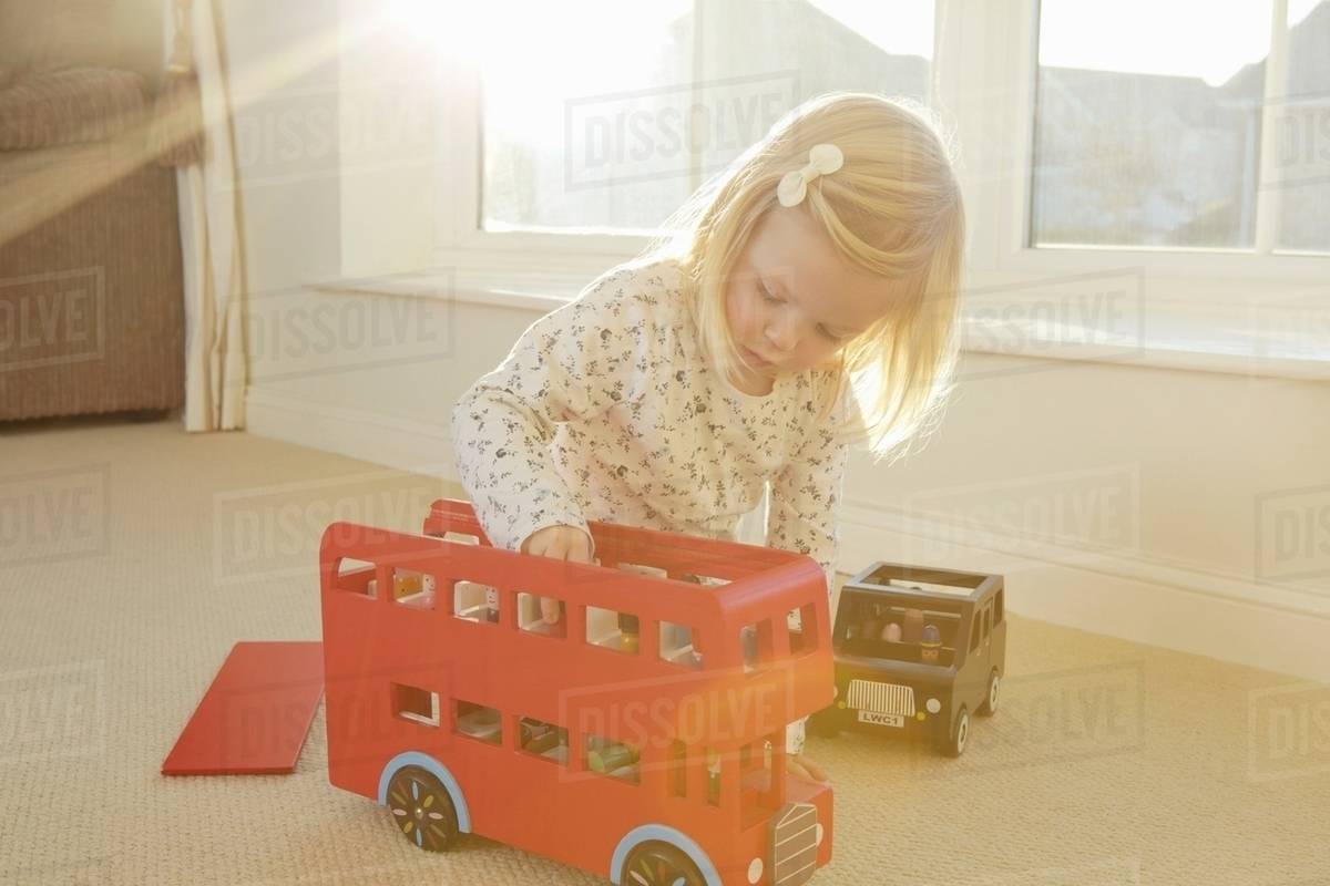 Girl playing with toy bus on floor - Royalty-free Stock Photo | Dissolve