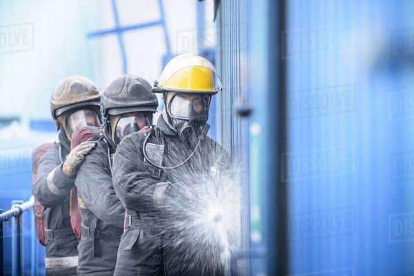 Three firefighters using hose in fire simulation training facility ...