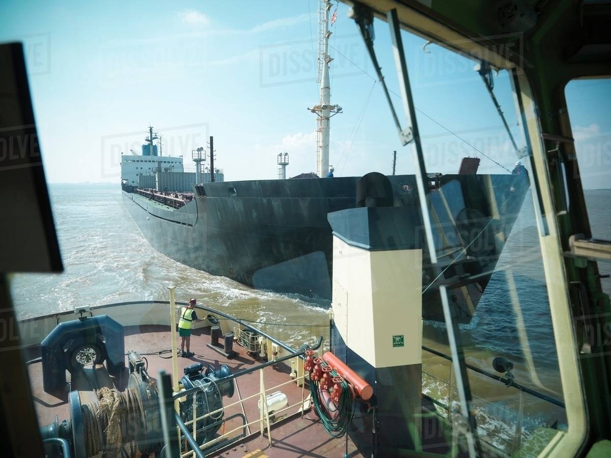 View from bridge of tugboat of sailor tyring tow lines to ship at sea ...