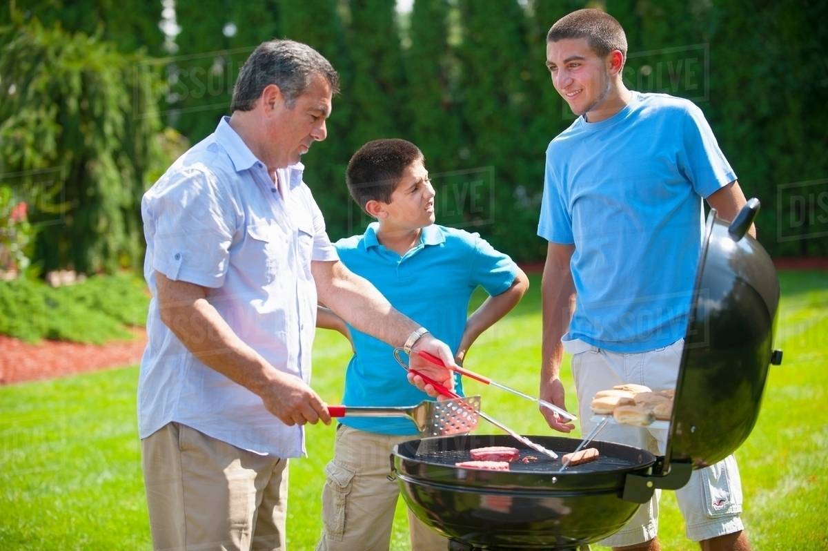 Father and sons grilling outdoors - Stock Photo - Dissolve