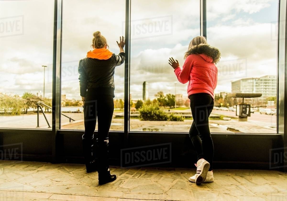 Two female friends looking out of window - Stock Photo - Dissolve