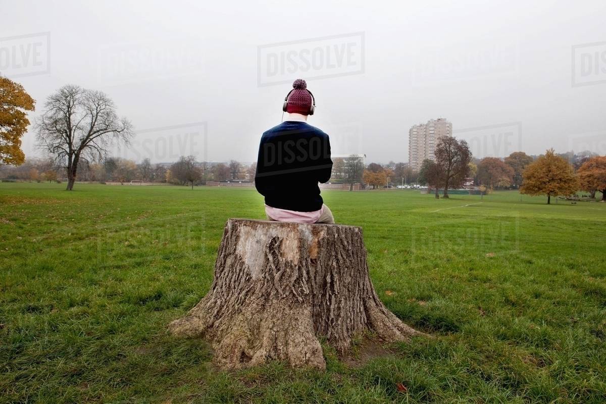 Man sitting on tree stump listening to music - Stock Photo - Dissolve