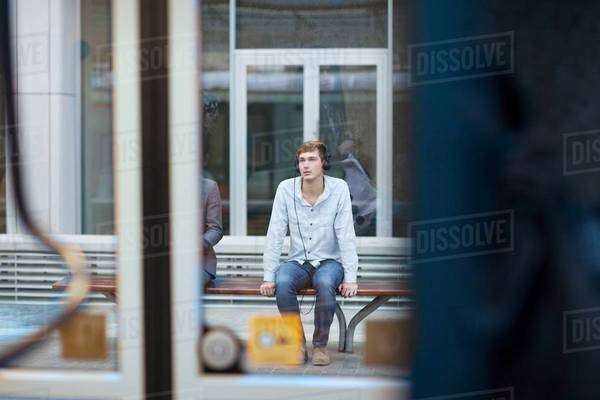 Young man sitting on train station bench - Stock Photo - Dissolve