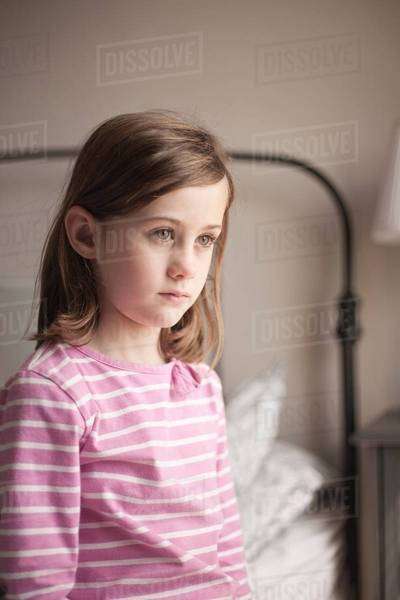 Girl sitting on bed staring - Stock Photo - Dissolve