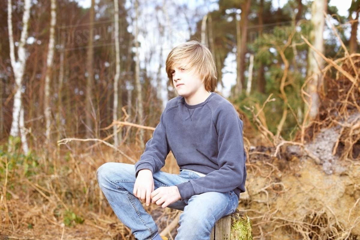 Boy sitting on tree stump in forest - Royalty-free Stock Photo | Dissolve