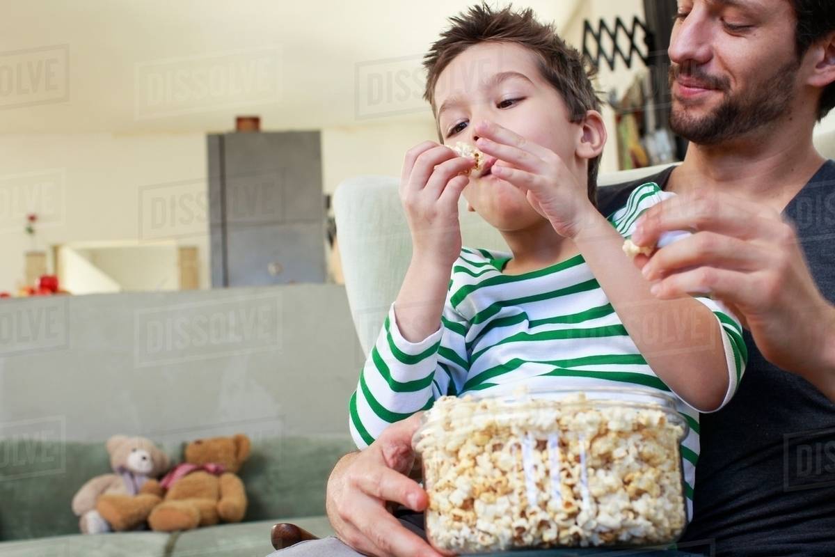 Father and son sharing popcorn in sitting room - Royalty-free Stock ...