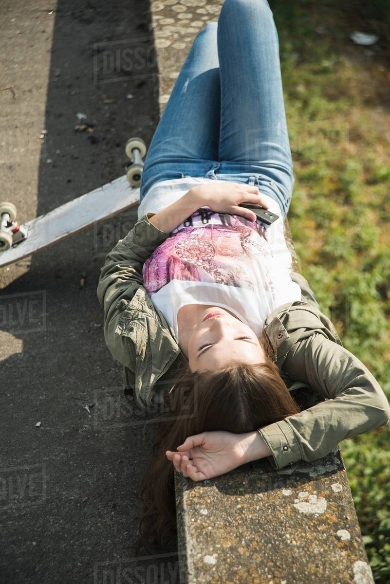 Young woman lying on wall asleep - Stock Photo - Dissolve