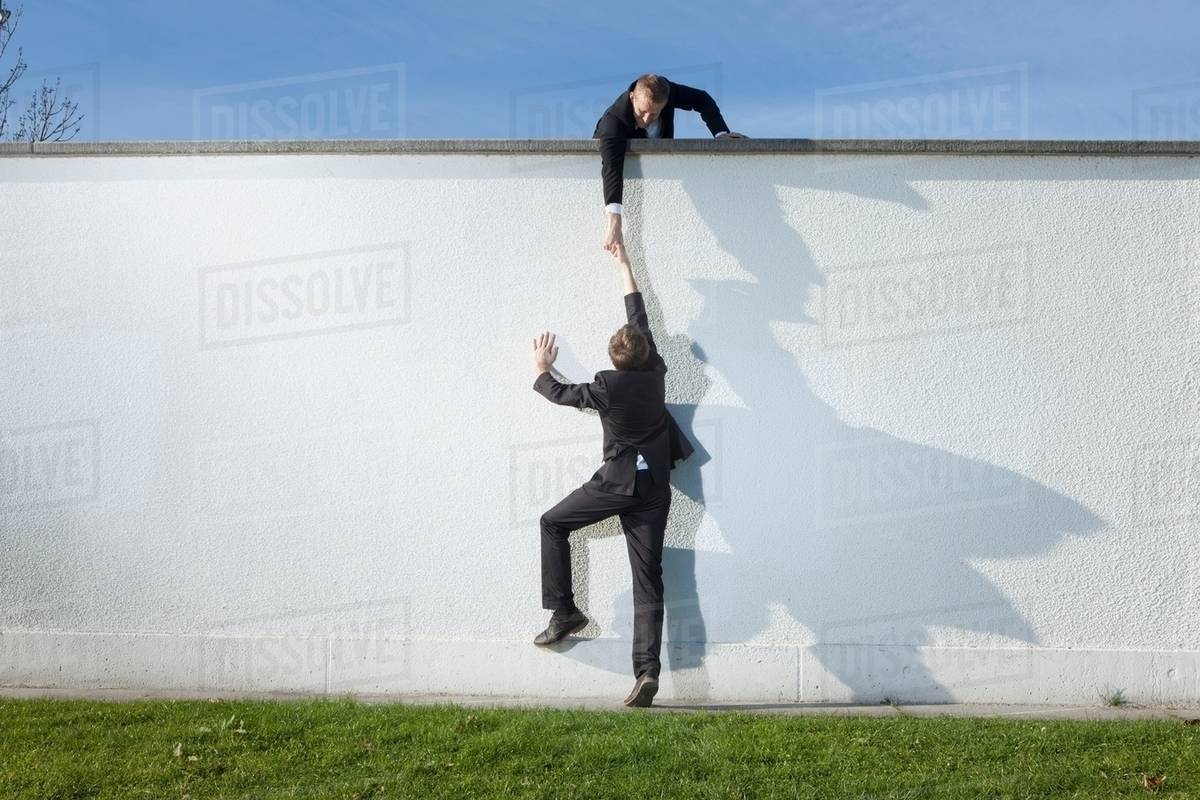 Businessman pulling colleague over wall - Royalty-free Stock Photo ...
