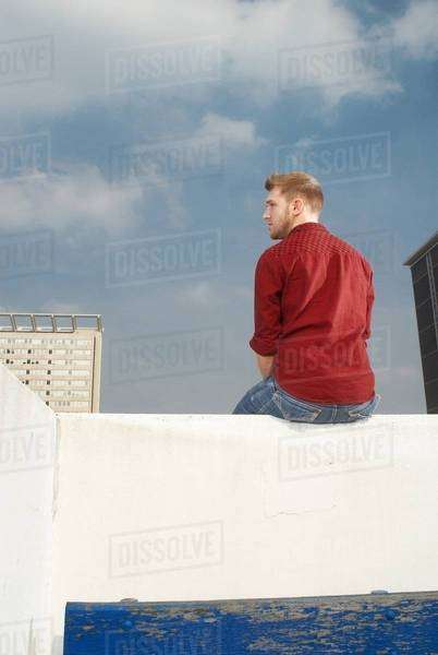 Man sitting on rooftop wall - Stock Photo - Dissolve