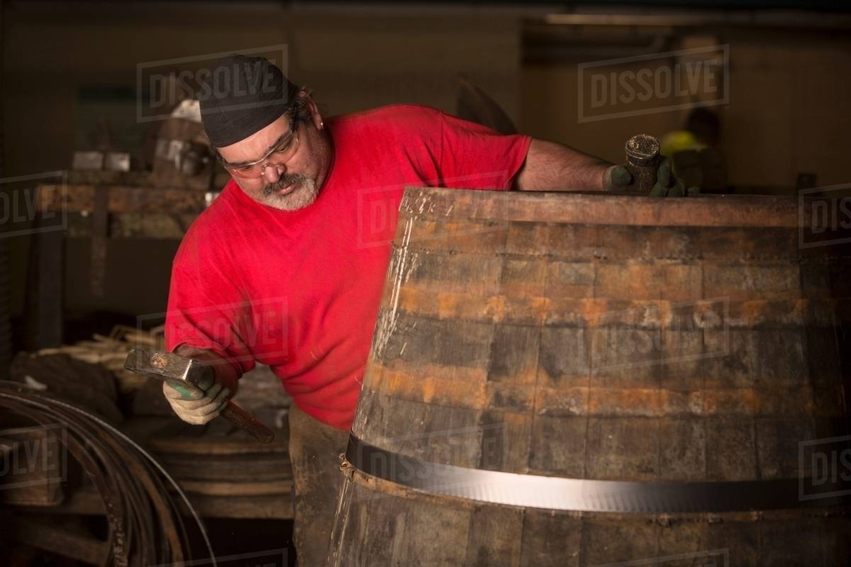 Male cooper using hammer in cooperage with whisky casks - Royalty-free ...