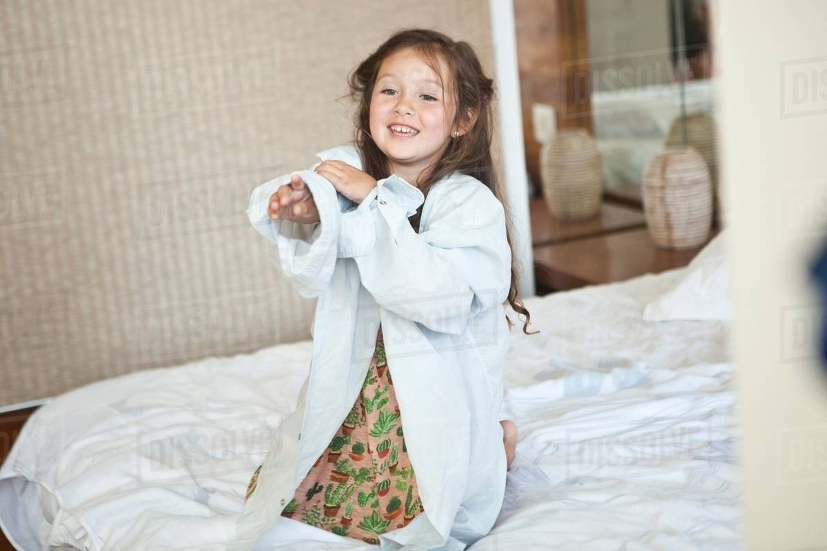 Portrait of young girl sitting on bed wearing oversized white shirt ...