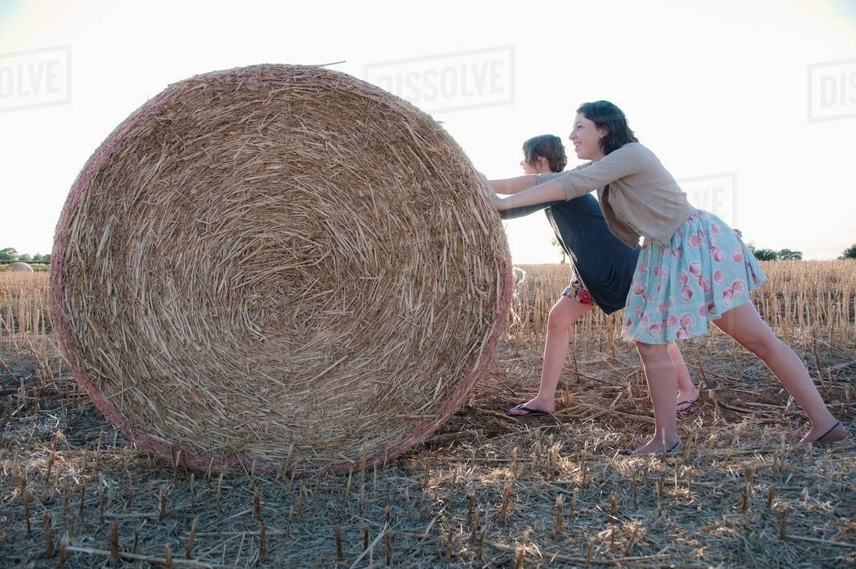 Girls pushing hay bale in field - Royalty-free Stock Photo | Dissolve