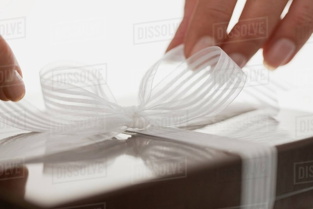 Close up of woman tying ribbon on gift - Stock Photo - Dissolve