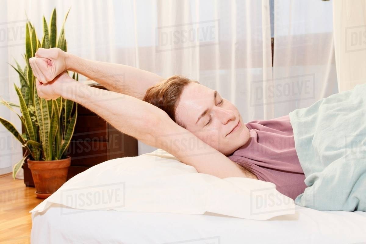 Smiling man stretching in bed - Royalty-free Stock Photo | Dissolve