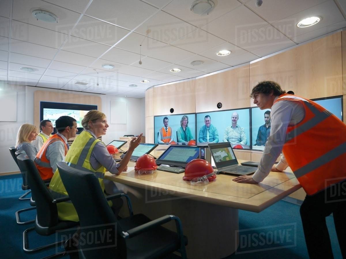 Staff members in meeting room with colleagues on video conference ...