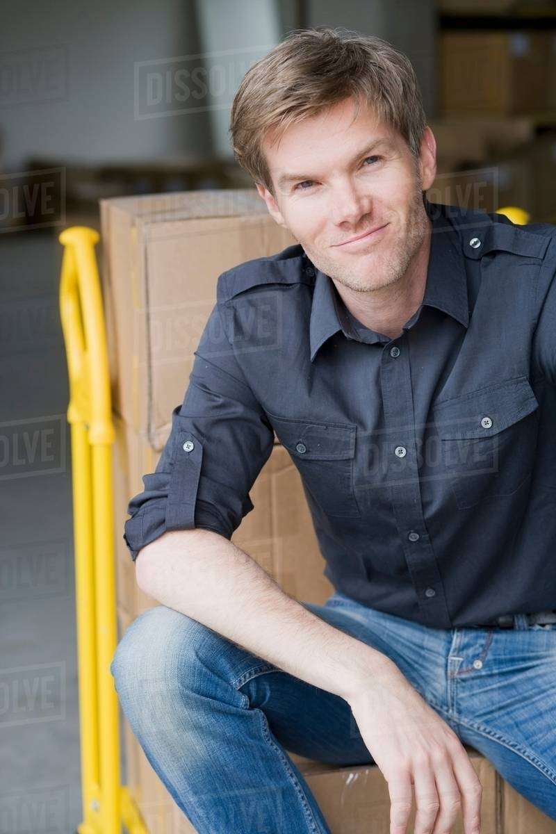 Smiling man sitting on boxes on dolly - Stock Photo - Dissolve