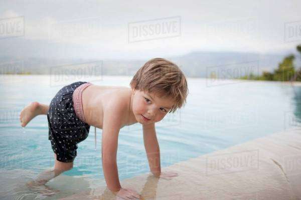 Boy climbing out of swimming pool - Stock Photo - Dissolve