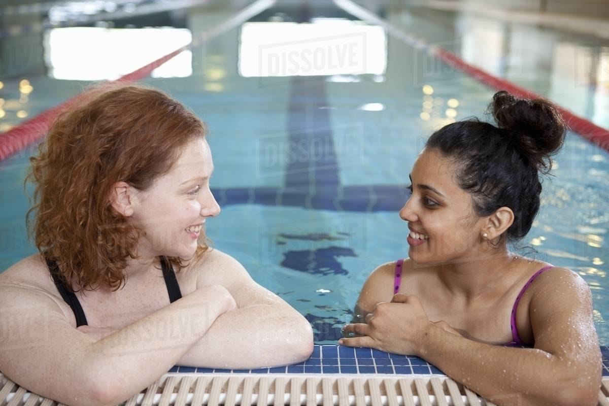 Women talking in indoor pool - Stock Photo - Dissolve