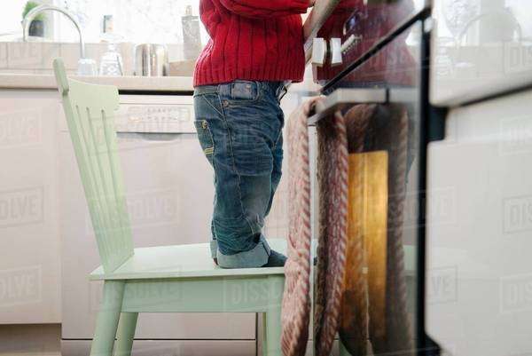 Boy standing on chair in kitchen - Stock Photo - Dissolve