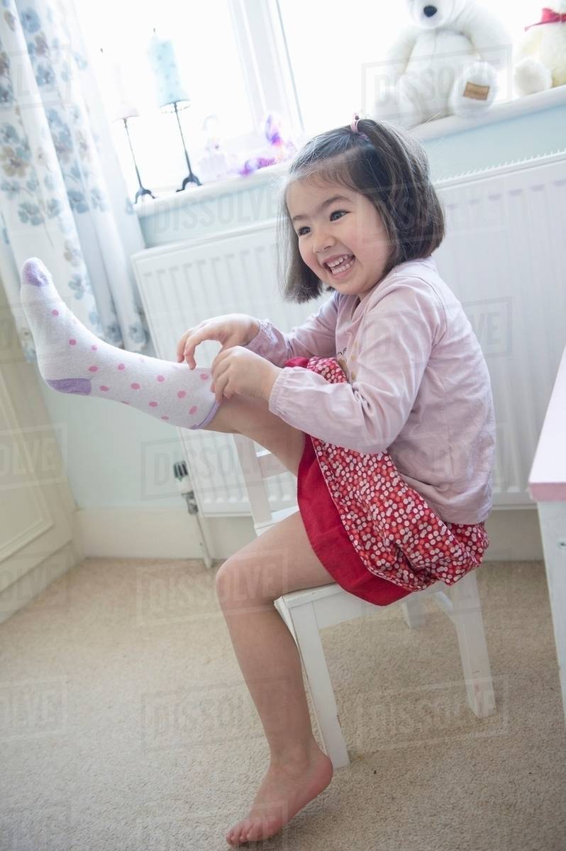 Young girl sitting on chair, pulling sock on - Stock Photo - Dissolve