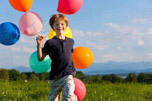 Boy with colorful balloons in grass - Stock Photo - Dissolve