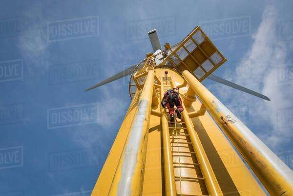 Engineer climbing ladder of wind turbine from boat at offshore windfarm ...