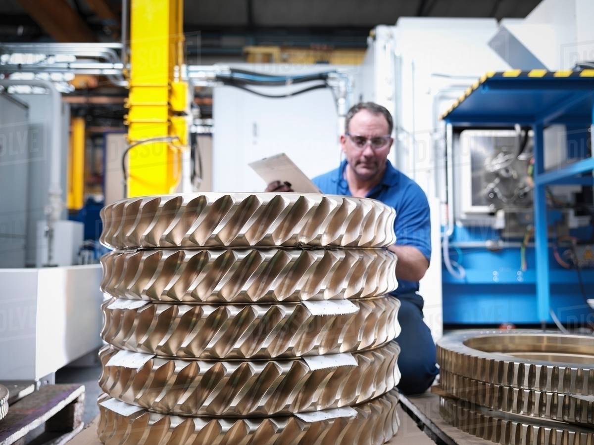 Engineer with bronze cogs in engineering factory - Stock Photo - Dissolve