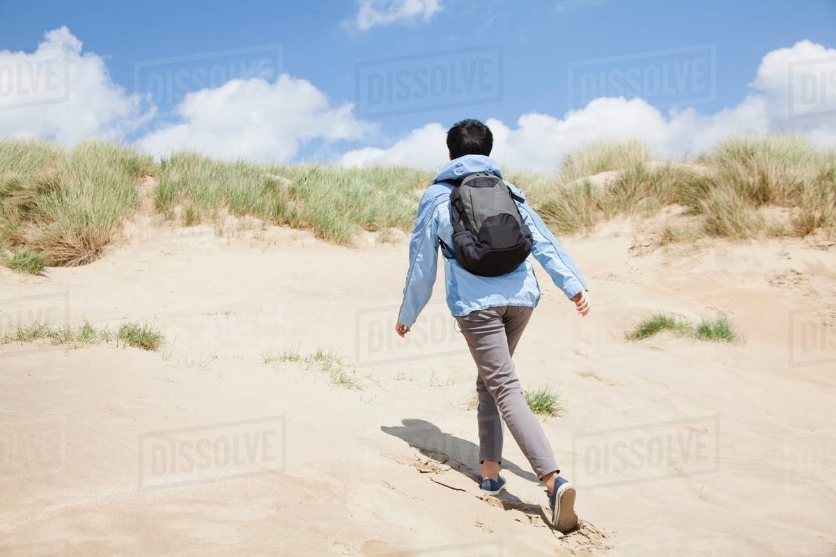 Rear view of mid adult female walker, walking up sand dune - Royalty ...