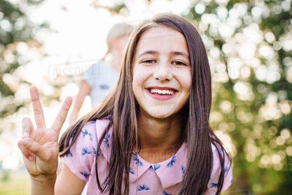 Girl smiling with peace sign in garden - Stock Photo - Dissolve