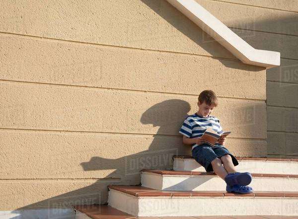 Boy sitting reading book in sunshine - Stock Photo - Dissolve