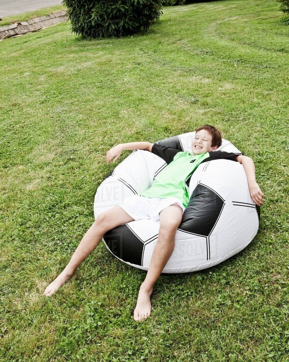 Boy relaxing on inflated giant football - Stock Photo - Dissolve