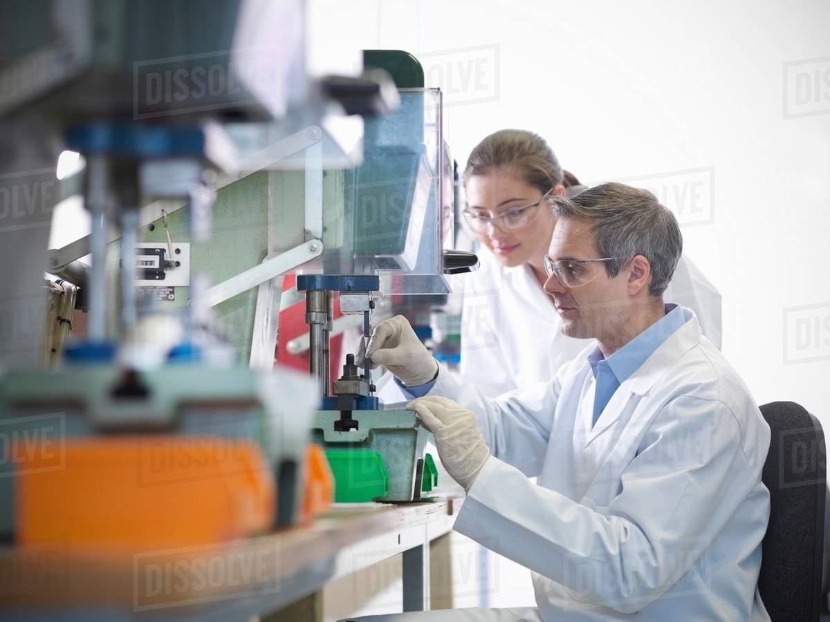 Male worker sat at workbench using equipment in laboratory, with female ...