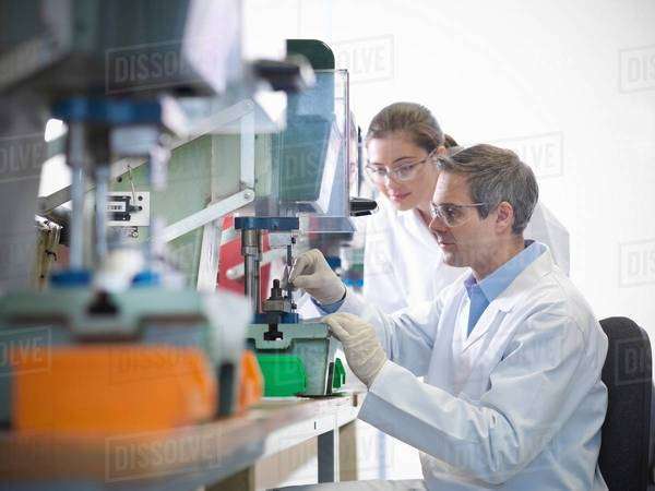 Male worker sat at workbench using equipment in laboratory, with female ...