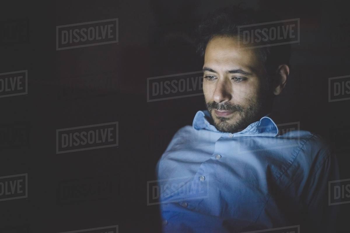 Young man leaning back looking down illuminated by laptop computer ...