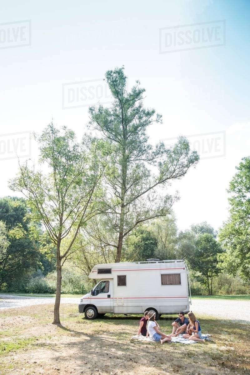 Group of young adults sitting on picnic blanket , relaxing, camper van ...