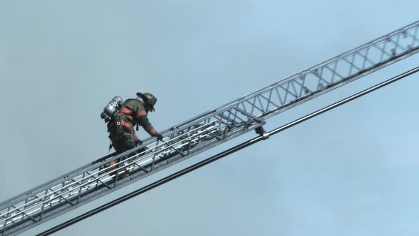Fireman climbing ladder from fire engine to fight large blaze below ...