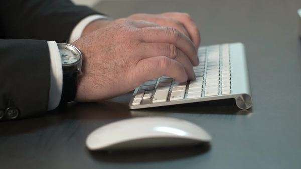 Close-up of a businessman working hard typing and using a mouse at a ...