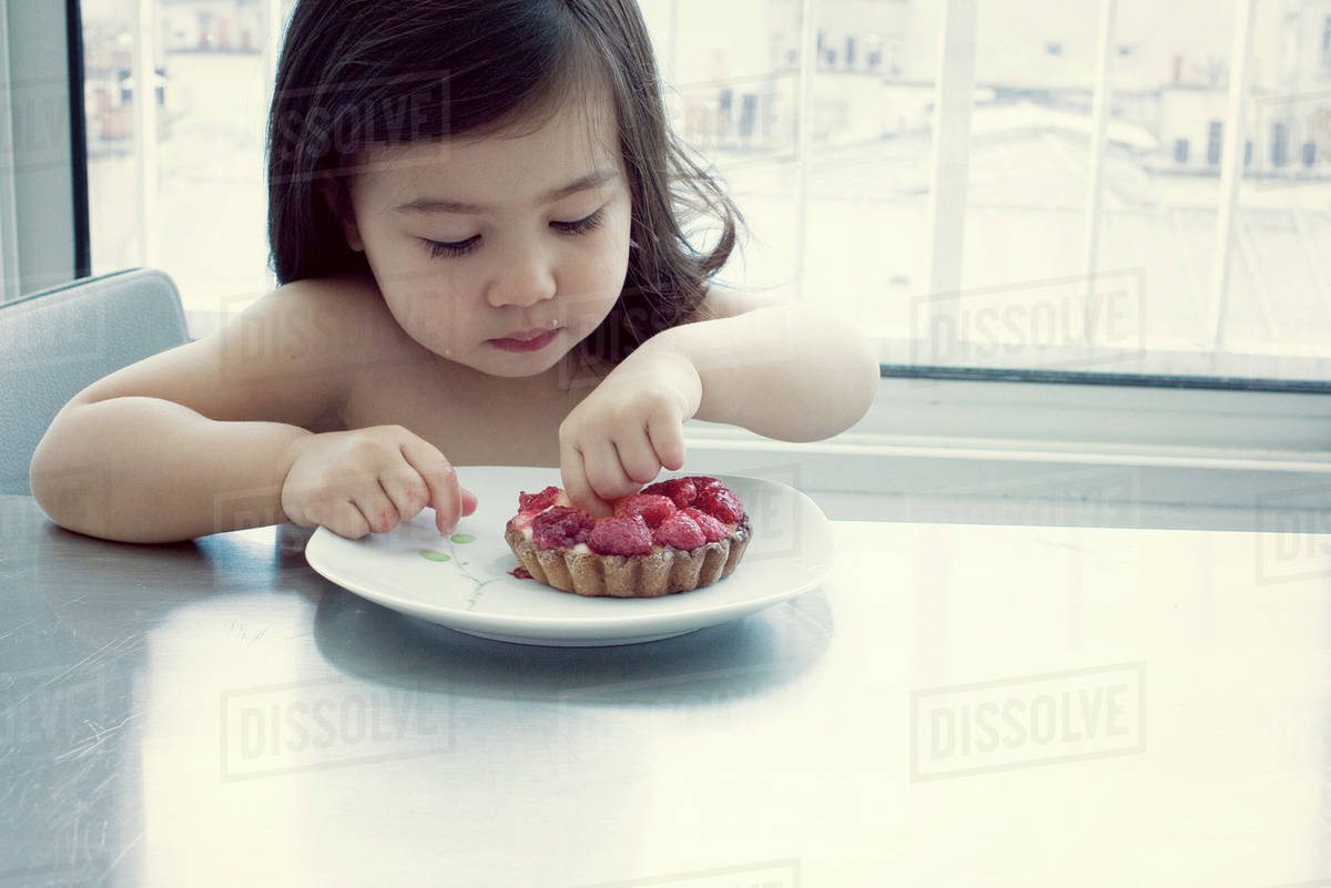 Little girl eating raspberry tart - Stock Photo - Dissolve