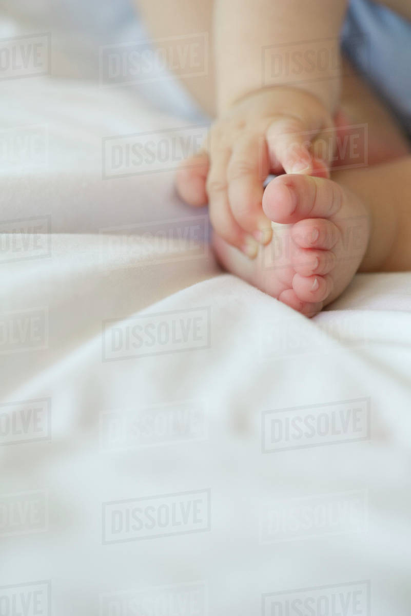 Baby touching its foot, cropped - Stock Photo - Dissolve