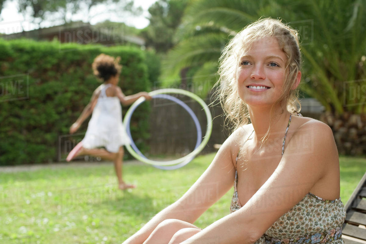 Woman relaxing outdoors, girl playing in background - Royalty-free ...